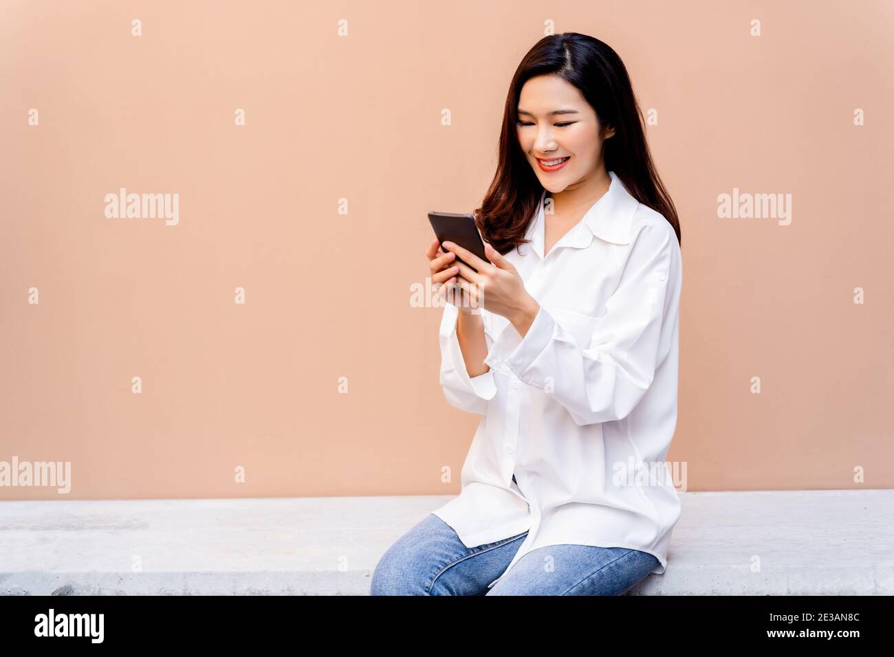 Asian woman texting on smartphone while sitting on a concrete bench ...
