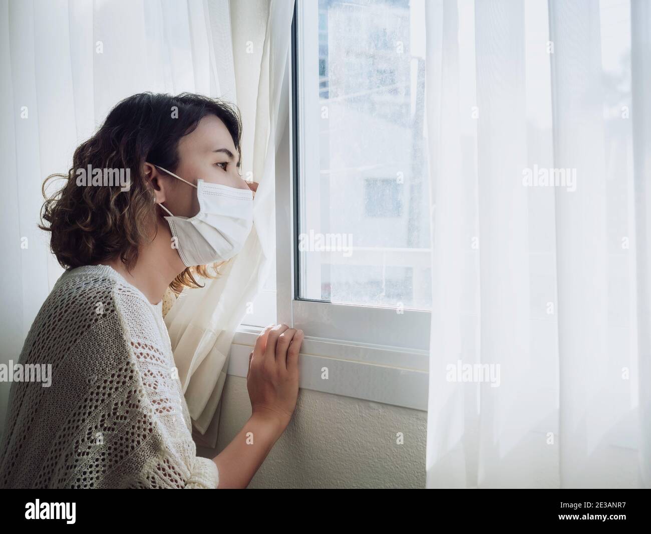 Beautiful lonely Asian woman wearing medical face mask looking out the ...