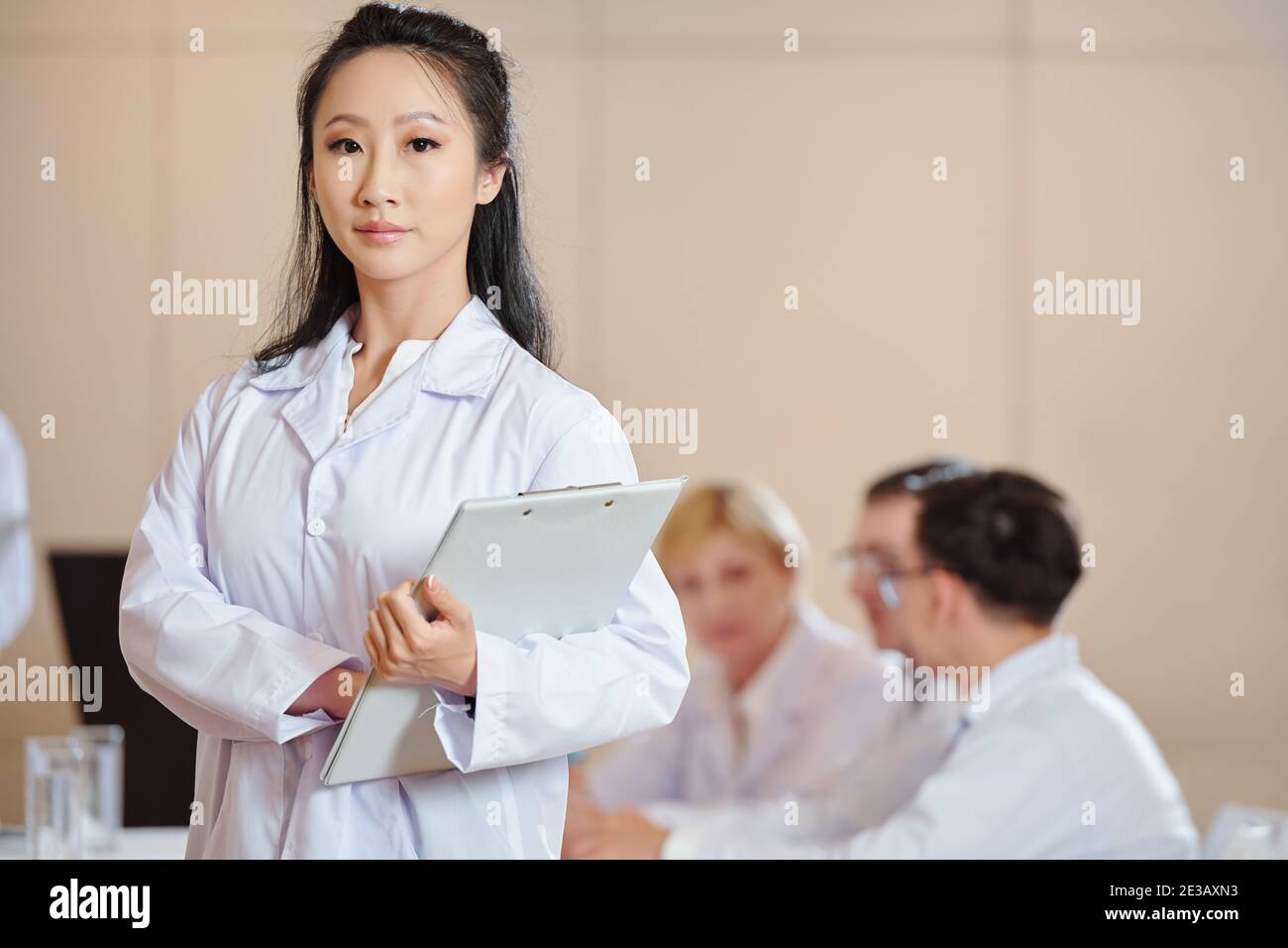 Serious young female Chinese scientist with clipboard standing in ...