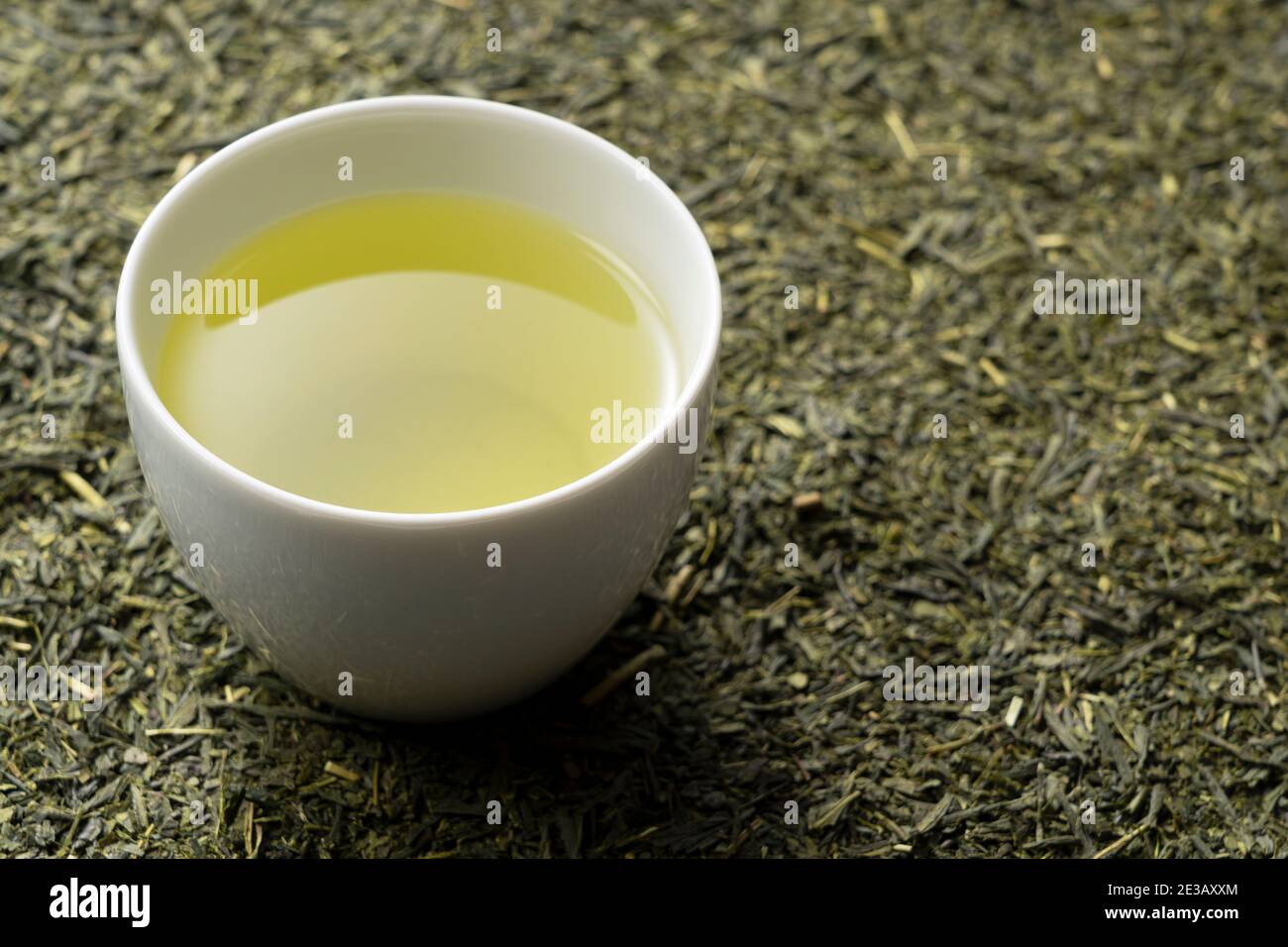 Tea leaves laid across the screen. Green tea in a white teacup placed ...