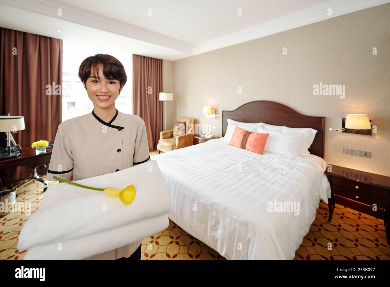 Portrait of pretty smiling young Vietnamese maid standing in hotel room ...