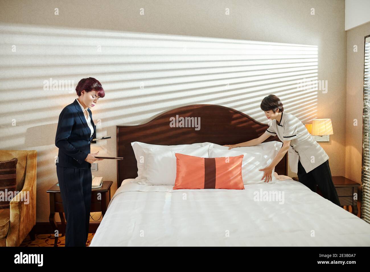 Hotel manager inspecting maid changing linen and making bed for guest ...