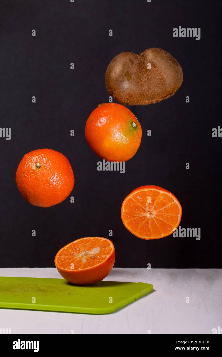 Tangerines and kiwis float above the table surface. Some are cut into ...