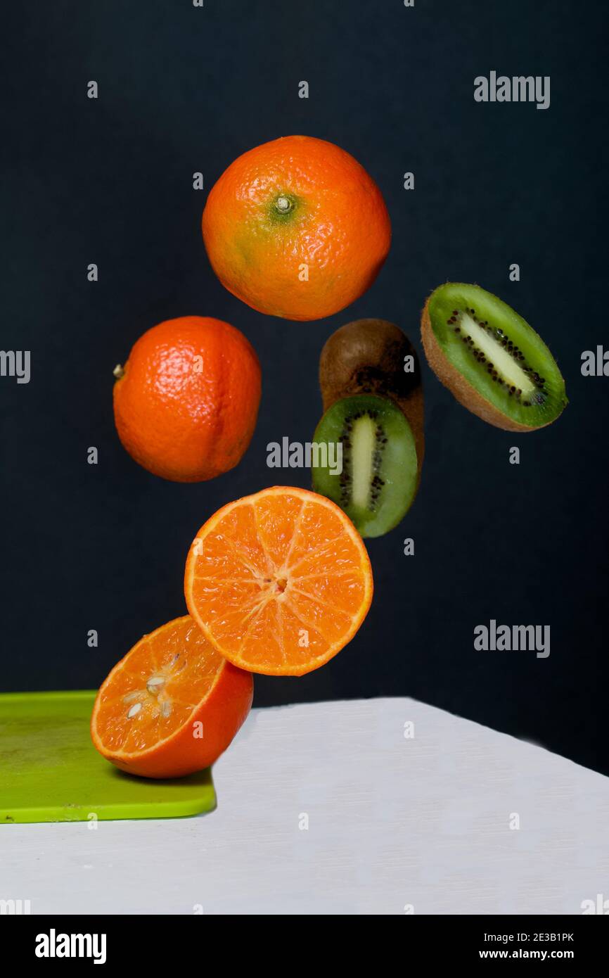 Tangerines and kiwis float above the table surface. Some are cut into ...