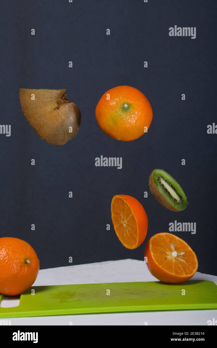 Tangerines and kiwis float above the table surface. Some are cut into ...