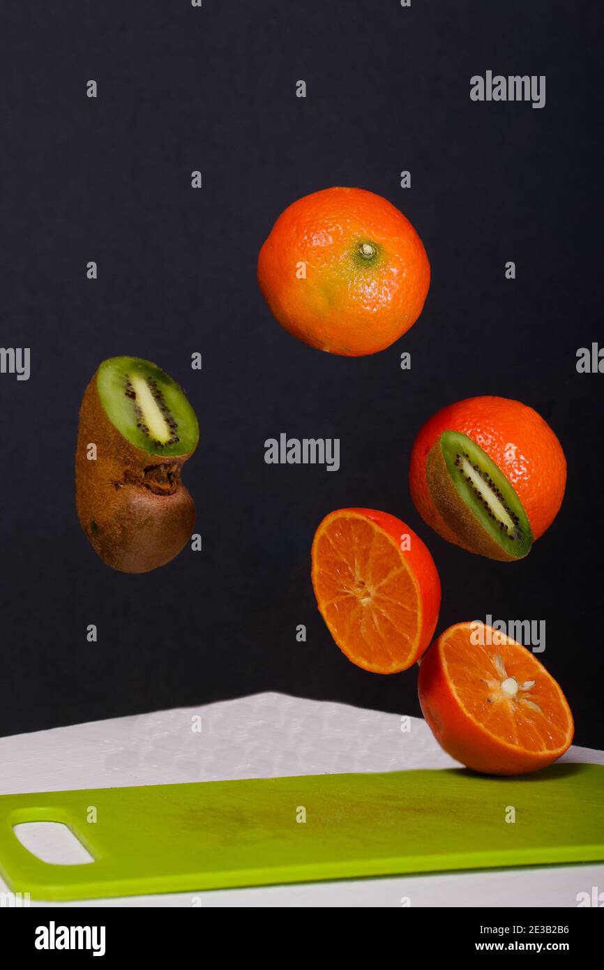 Tangerines and kiwis float above the table surface. Some are cut into ...
