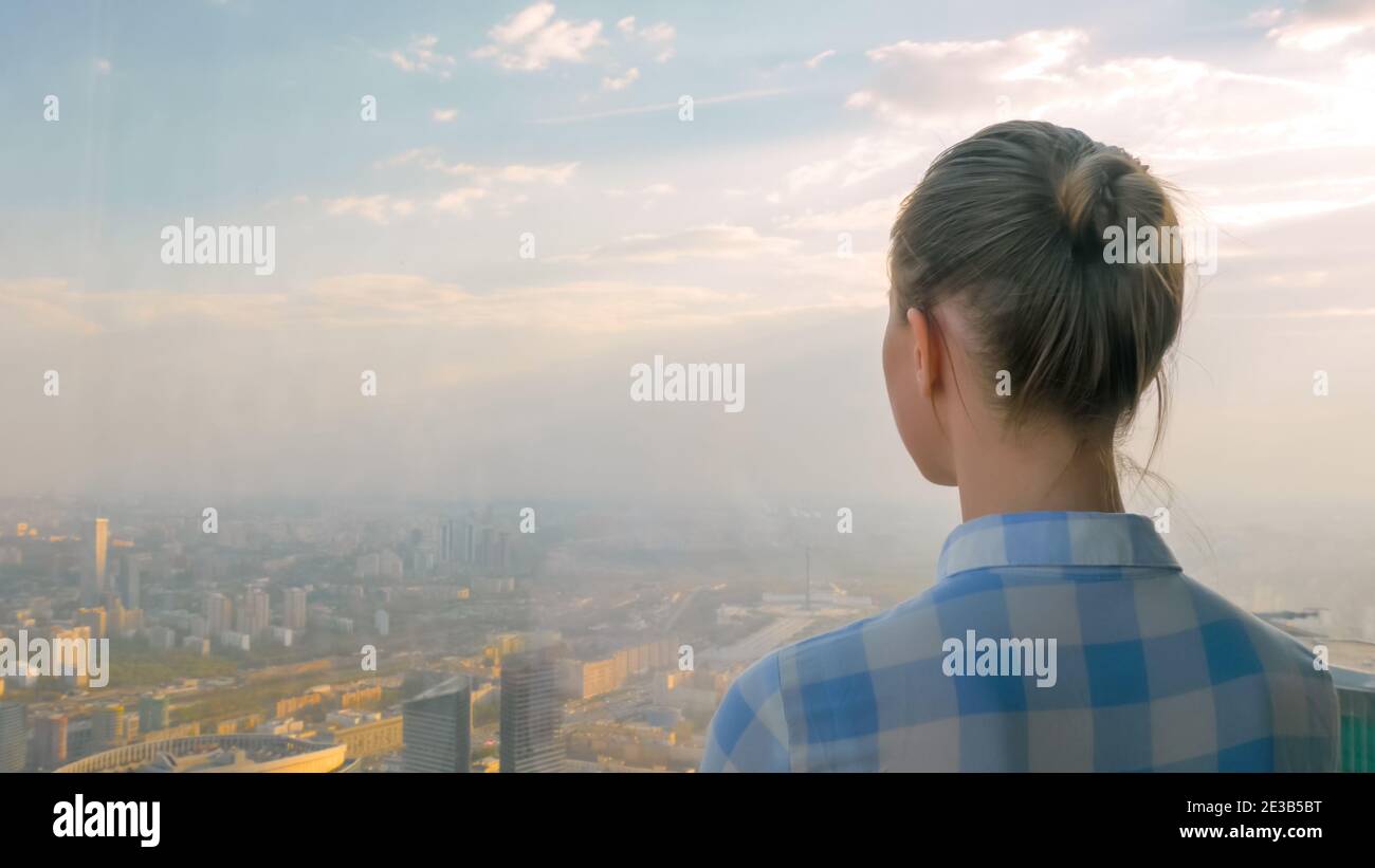 Back view of woman looking at cityscape through window of skyscraper ...