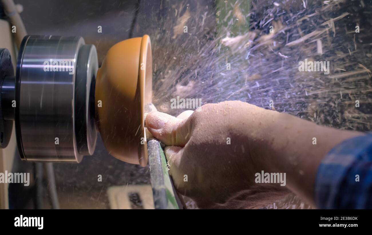Carpenter using chisel for shaping wood piece on lathe - side view ...