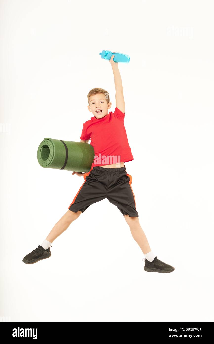 Adorable male child holding exercise mat and refreshing sports drink ...