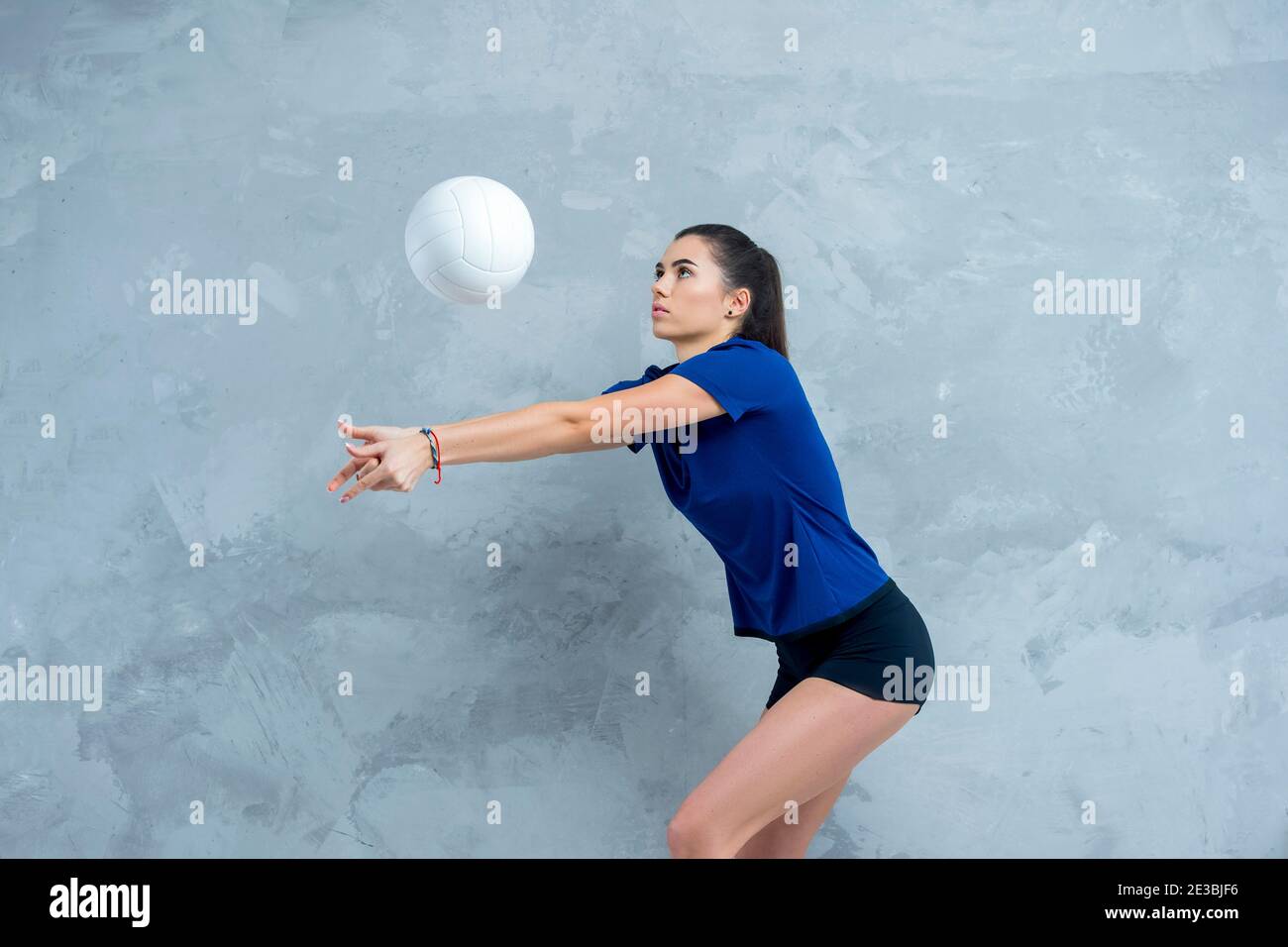 Volleyball girl hold and kick ball in blue costume on grey concrete ...