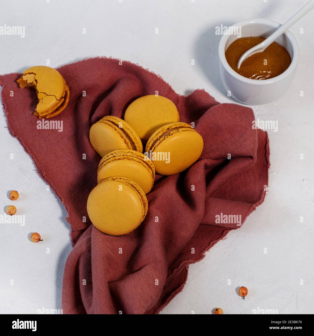 Apricot macarons lying on a white table top, next to it a white bowl ...