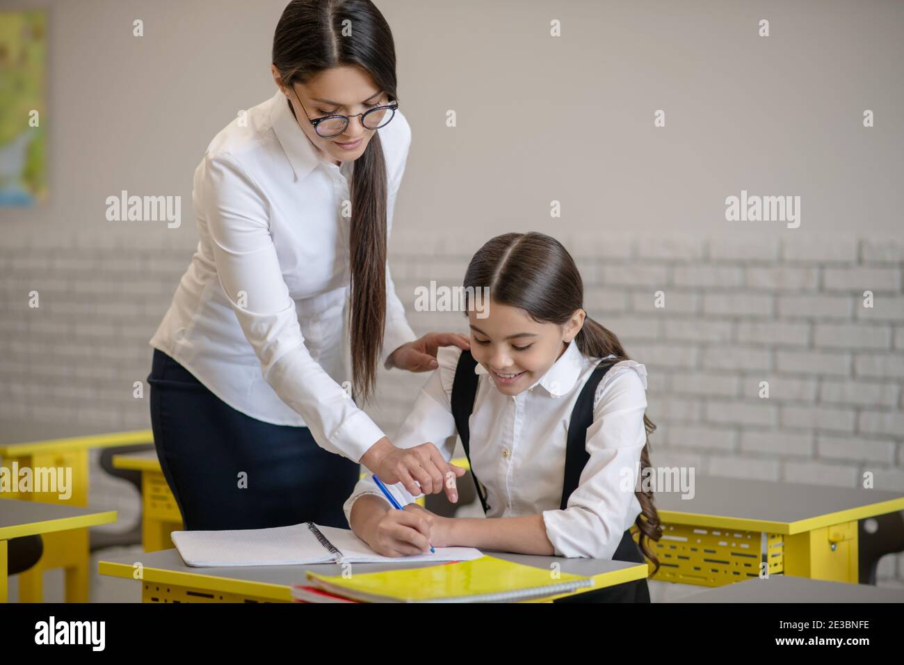 Woman with glasses bending over schoolgirl at desk Stock Photo - Alamy