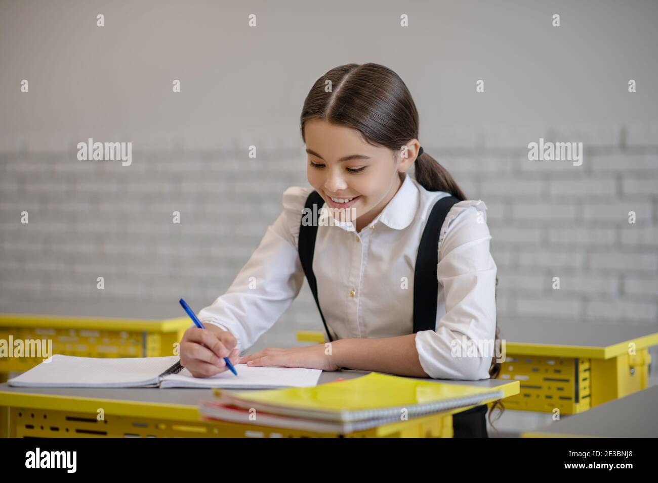 Girl in school uniform writing at desk Stock Photo - Alamy