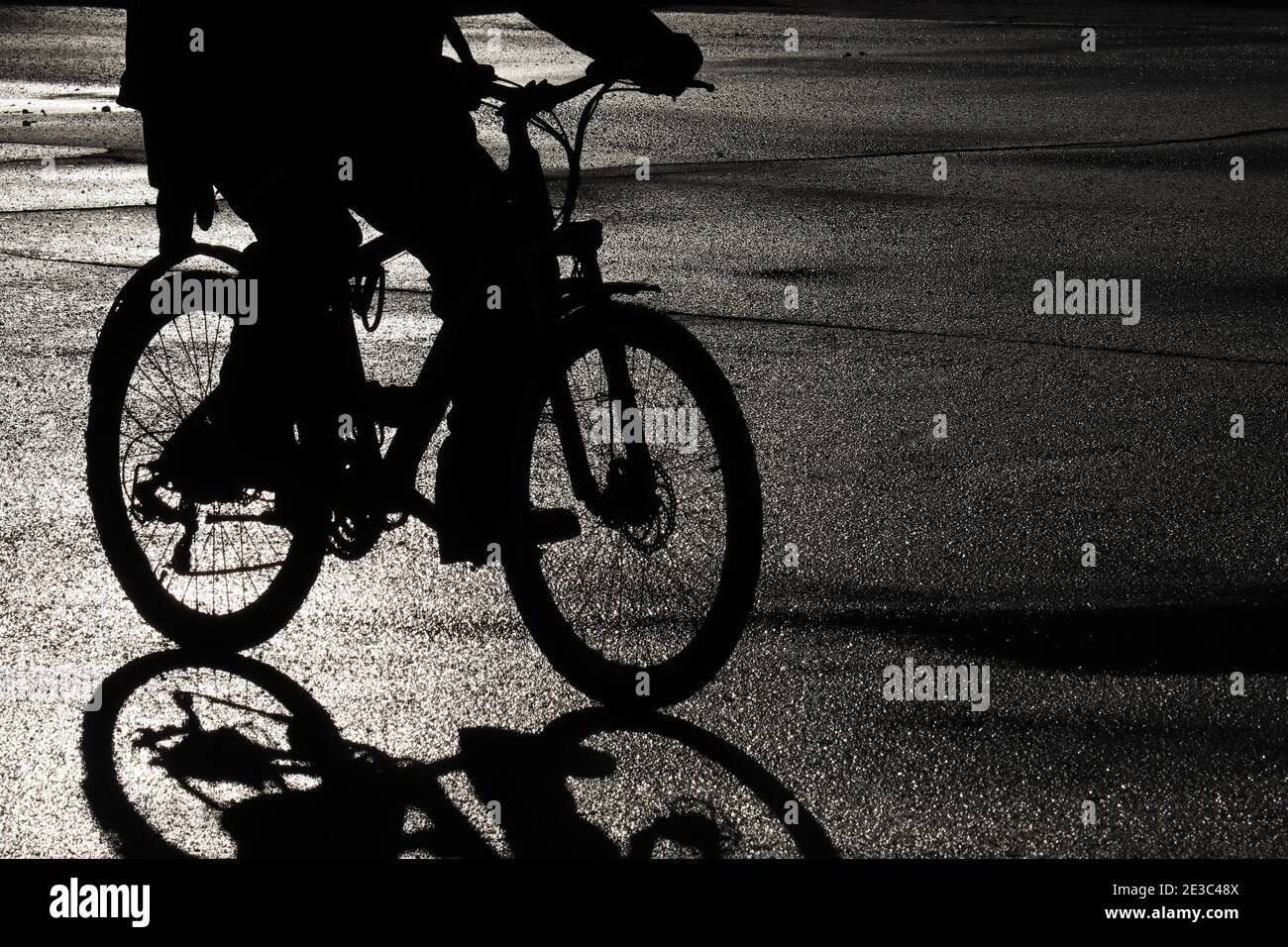 Black silhouette of a cyclist on the wet road. Person riding a bicycle ...
