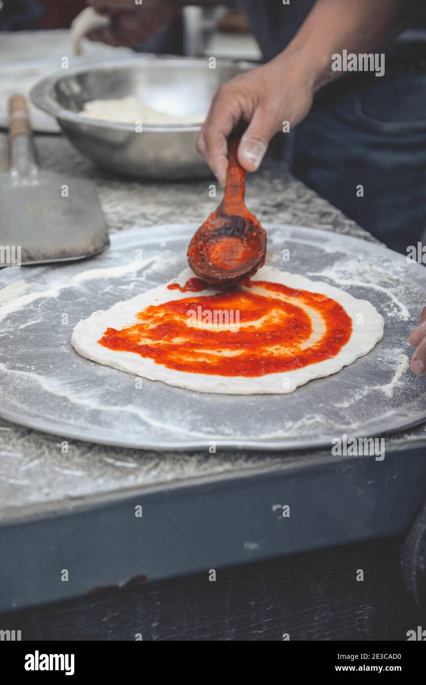Vertical selective focus shot of a hand saucing the dough of pizza with ...