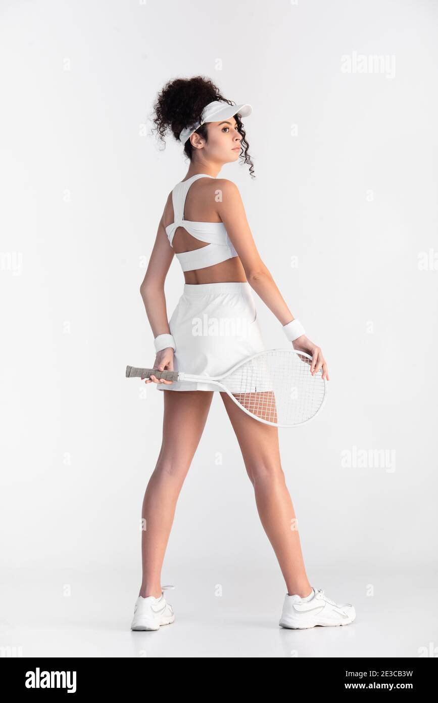 full length of curly young player in sportswear holding tennis racket ...