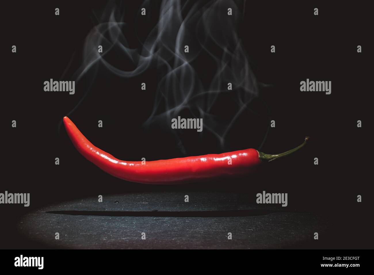 Red hot chili pepper on a dark black surface with smoke emphasizing the ...