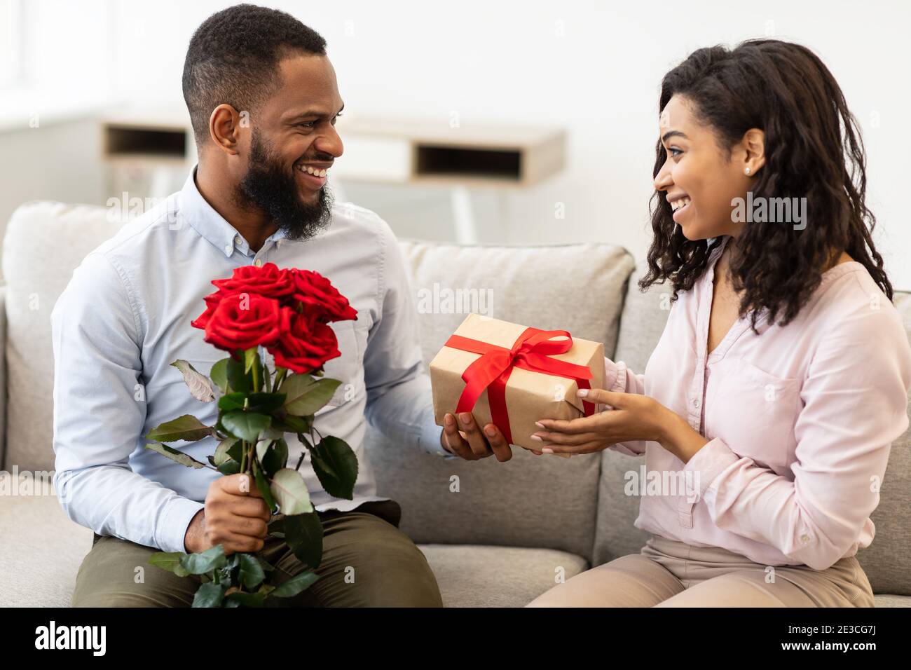 Happy black man giving red roses and box to woman Stock Photo - Alamy