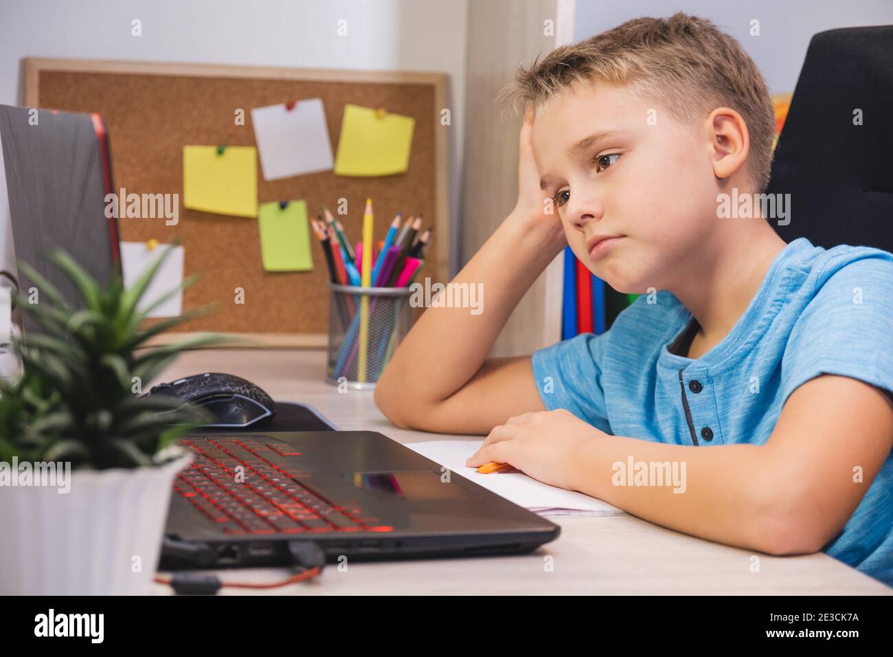Sad schoolboy studies at home with laptop and does school homework ...