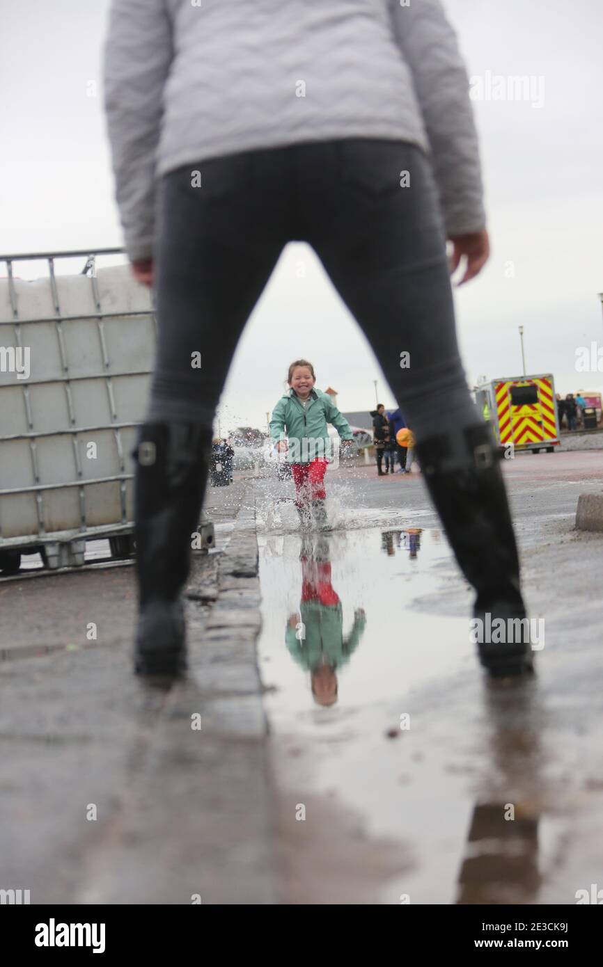 Young child having fun running through a puddle on Ayr Seafront ...