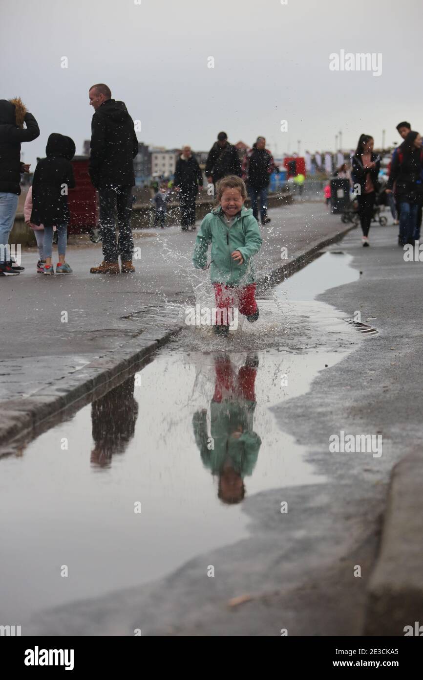 Young child having fun running through a puddle on Ayr Seafront ...
