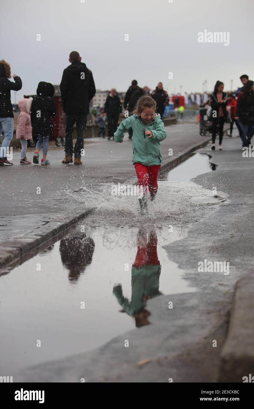 Young child having fun running through a puddle on Ayr Seafront ...