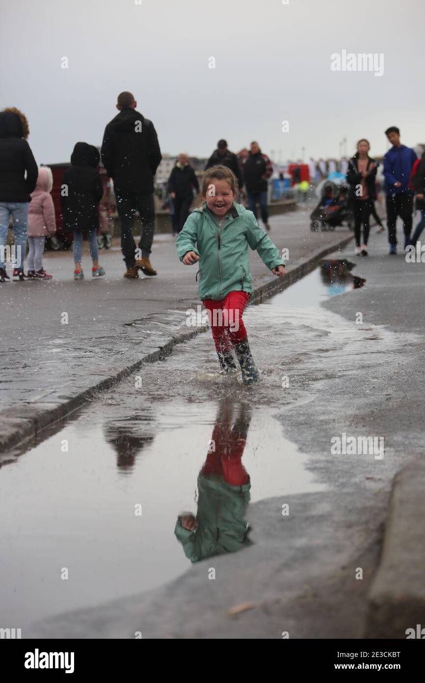 Young child having fun running through a puddle on Ayr Seafront ...