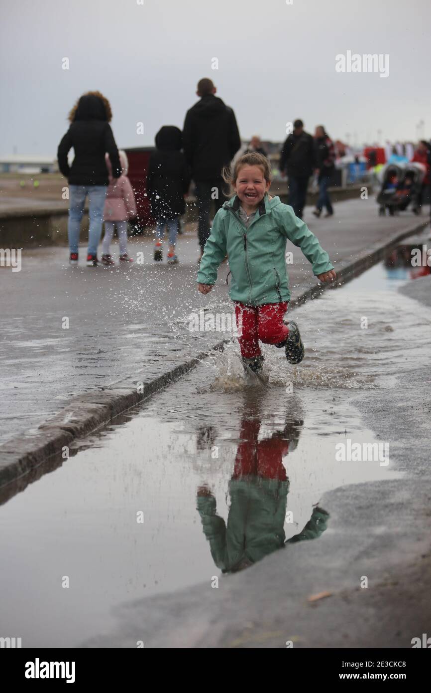 Young child having fun running through a puddle on Ayr Seafront ...