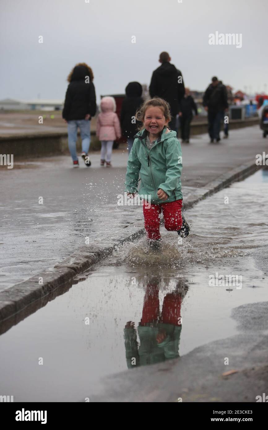 Young child having fun running through a puddle on Ayr Seafront ...