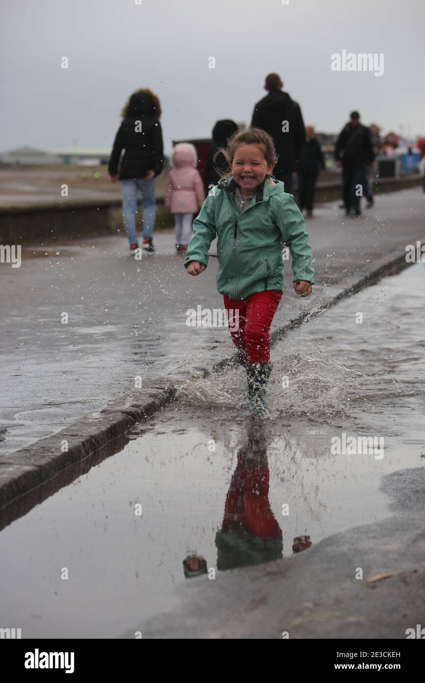 Young child having fun running through a puddle on Ayr Seafront ...