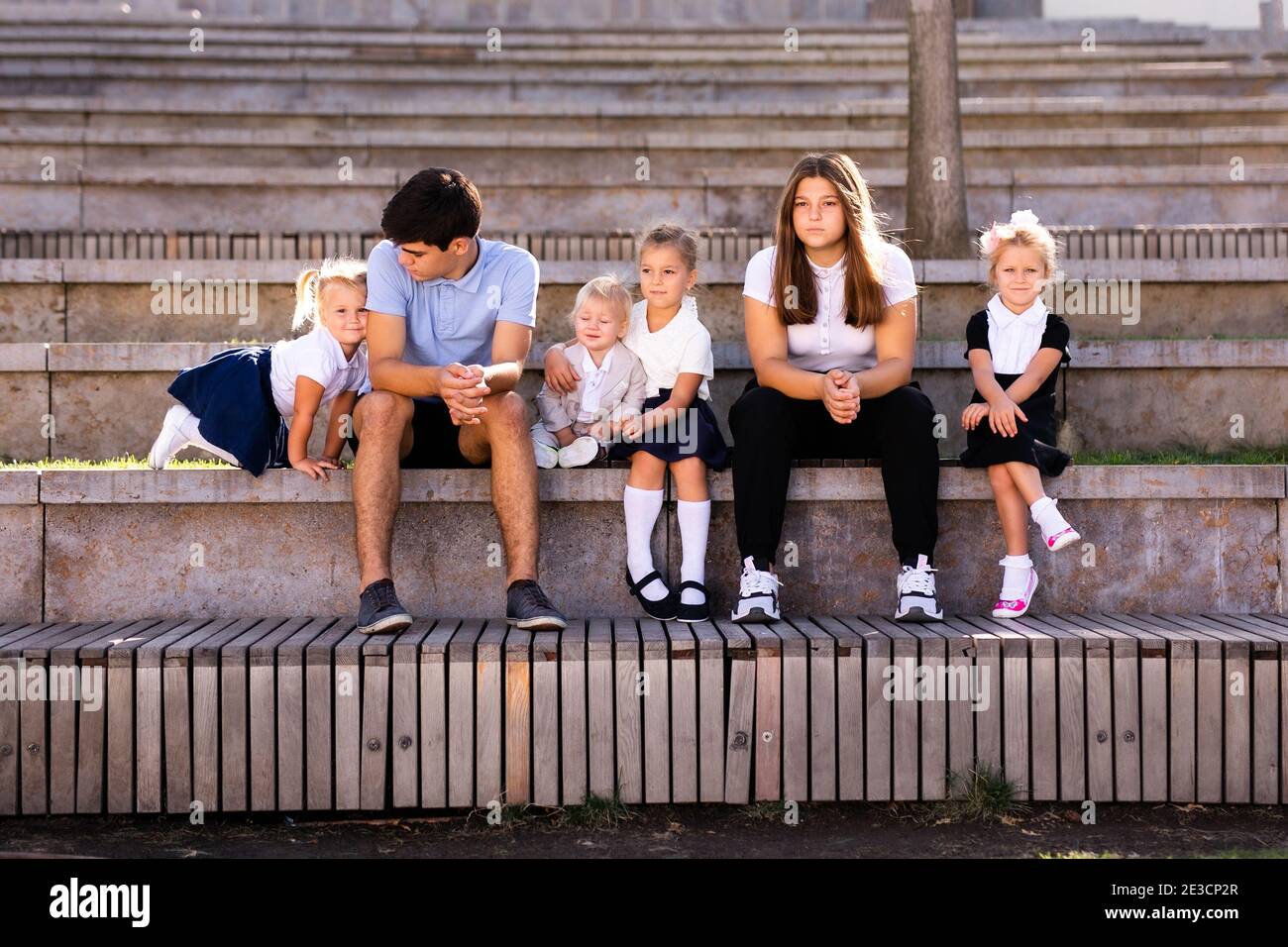 Children of different ages in school uniforms sitting on the steps ...
