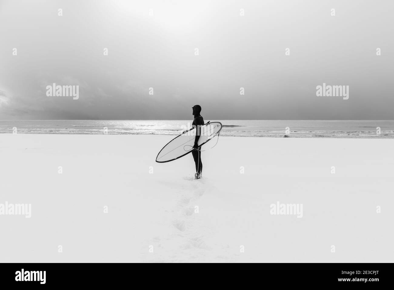 Winter and surfer with surfboard. Snowy beach and surfer in wetsuit ...