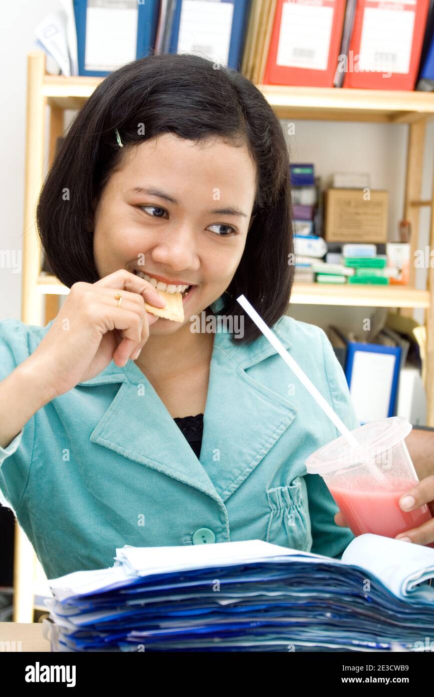 asian female employee eating snack and drinking while at work Stock ...