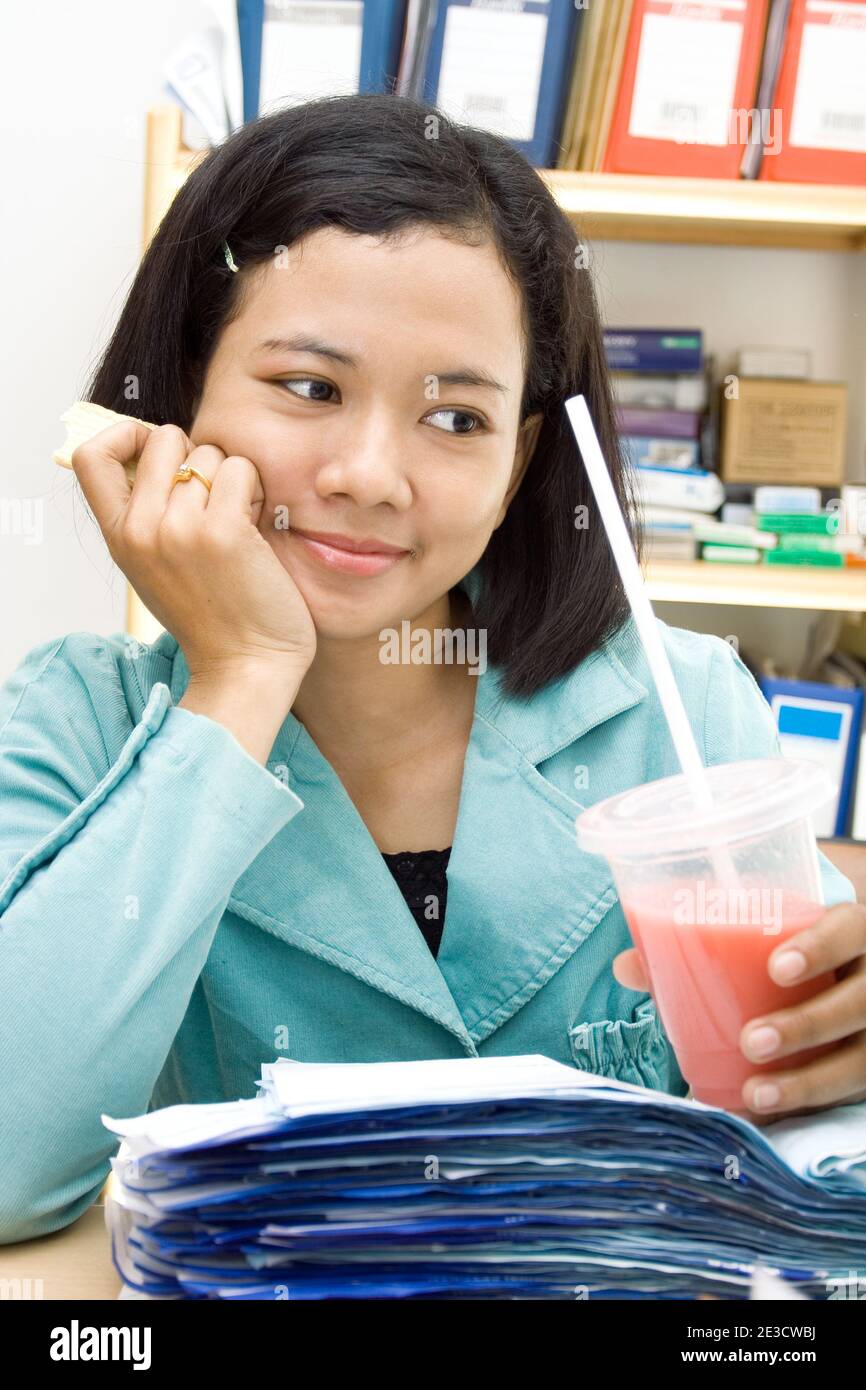asian ethnic female employee eating snack and drinking while at work ...
