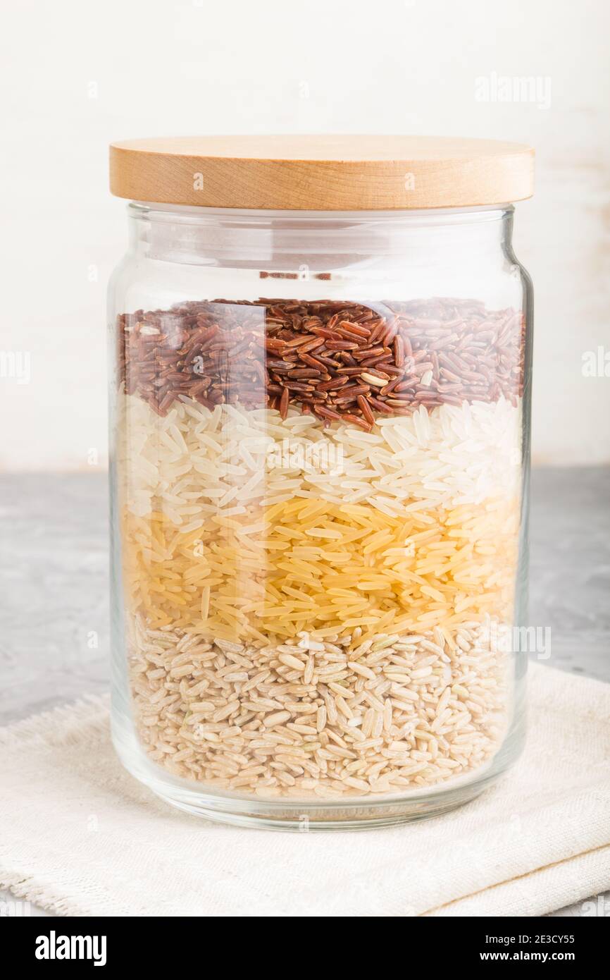 glass jar with different kinds of rice poured in layers on a gray and ...