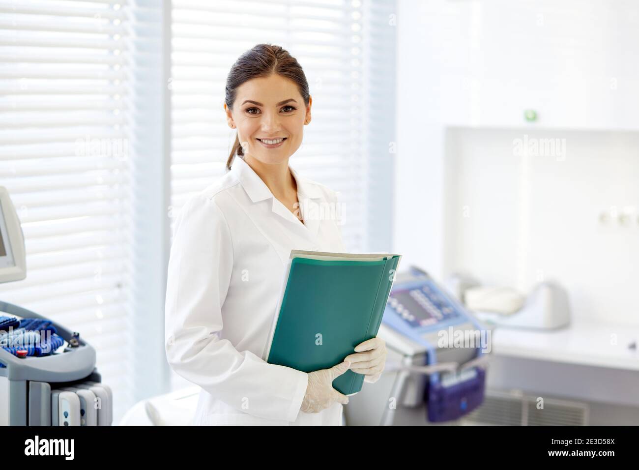 female doctor with document case in hands and looking at camera, posing ...