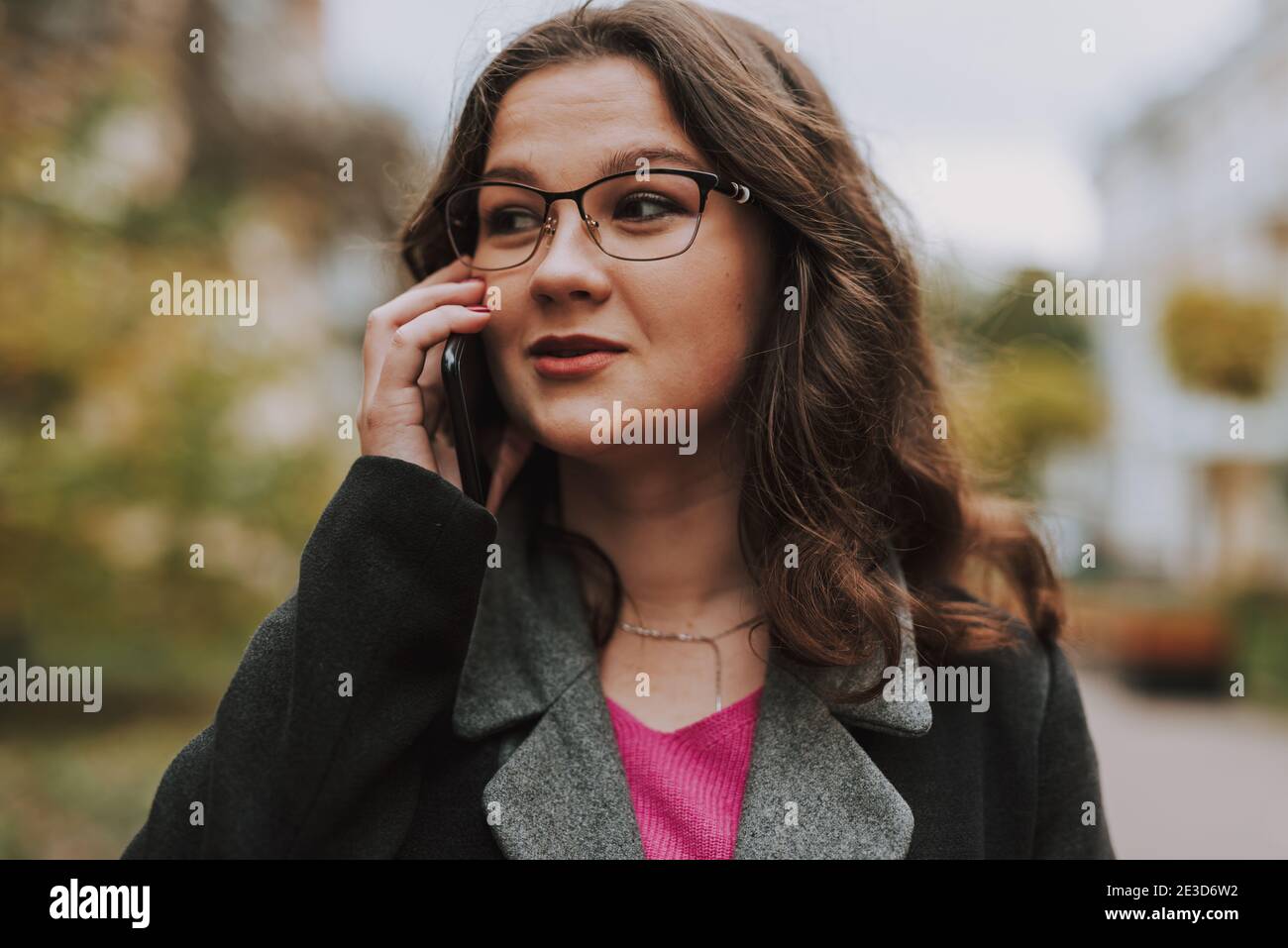 Calm young woman looking into the distance and talking on the phone ...