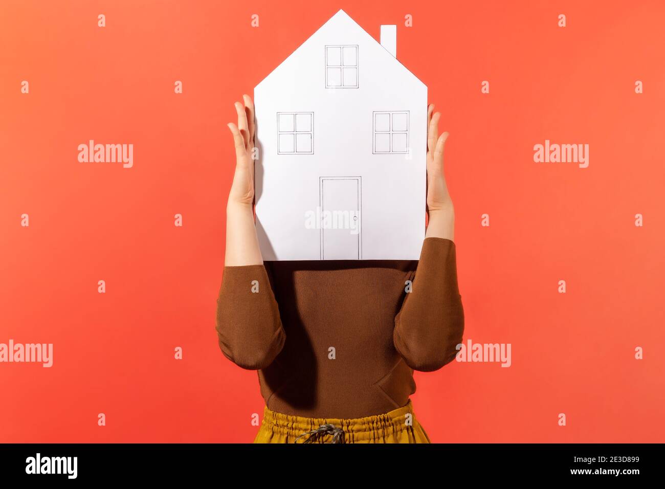 Woman hiding her face behind paper house with drawn windows and door ...