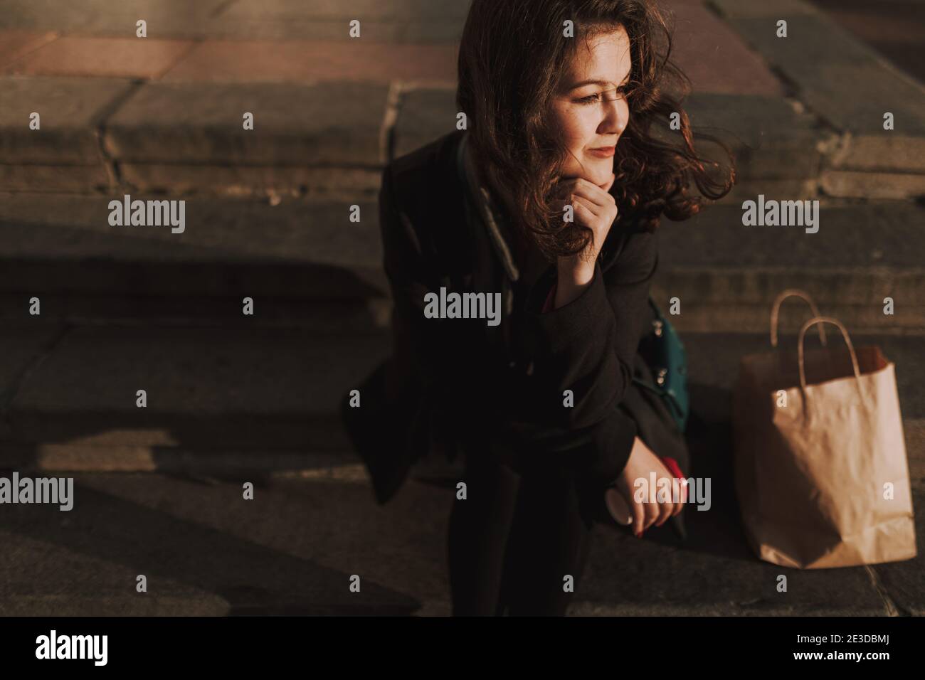 Happy pretty lady sitting on steps and looking away in the city during ...