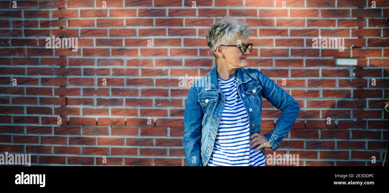 Senior woman standing outdoors against brick wall background. Copy ...