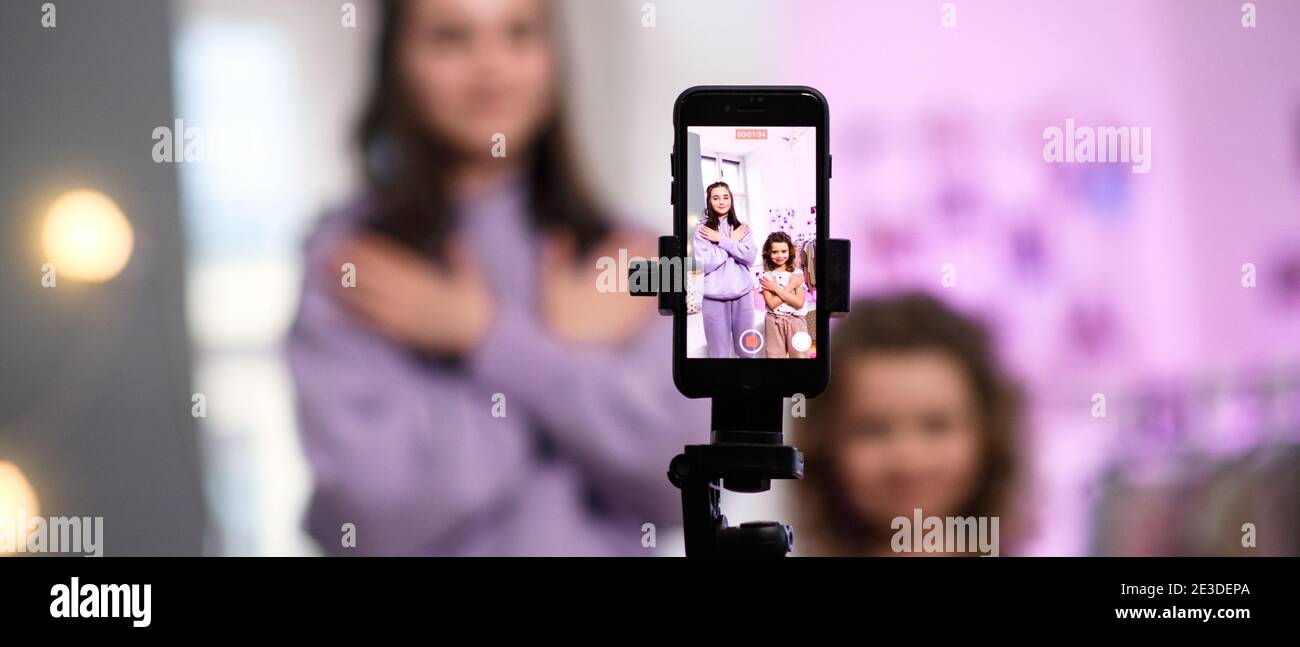 Sisters indoors at home, making video with smartphone. Lockdown concept ...