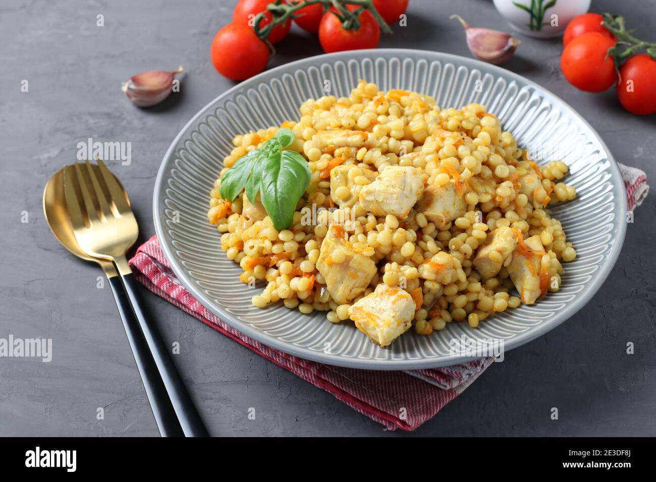 Homemade ptitim pasta with chicken and vegetables on dark gray table ...