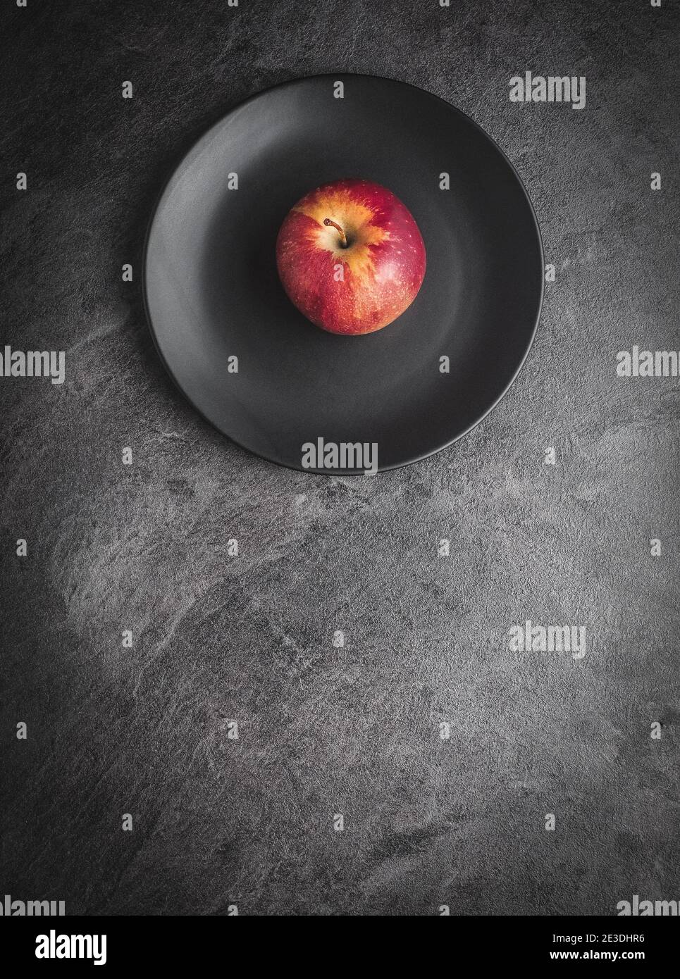 Red apple on black plate and on grey table. Dark and moody. Overhead ...