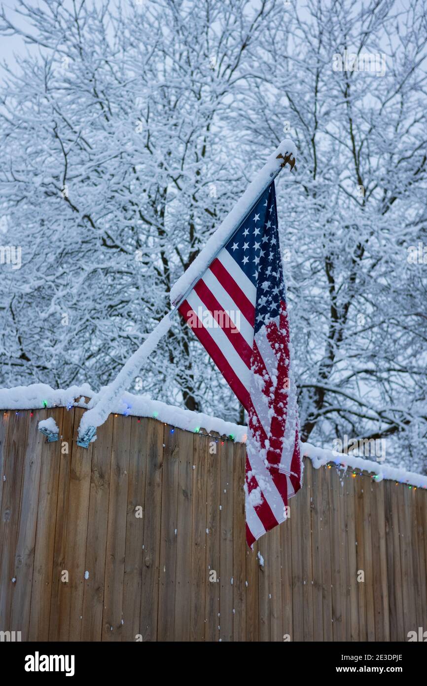 The American Flag, displayed on a wooden fence, is covered with snow ...