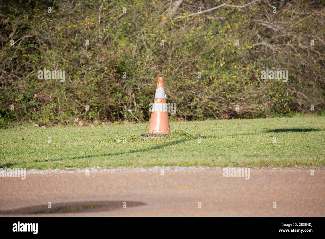 Orange caution cone with two white stripes in a yard near bushes Stock ...