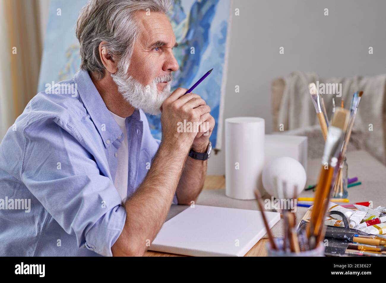 artist sitting behind table and thinking what to draw, paint. elderly ...