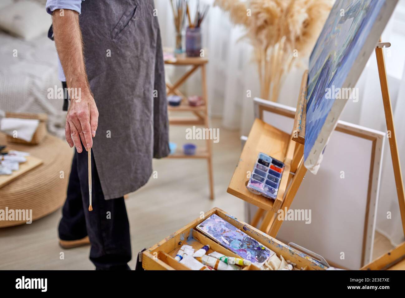 male painter man in apron during work process, male using paintbrushes ...