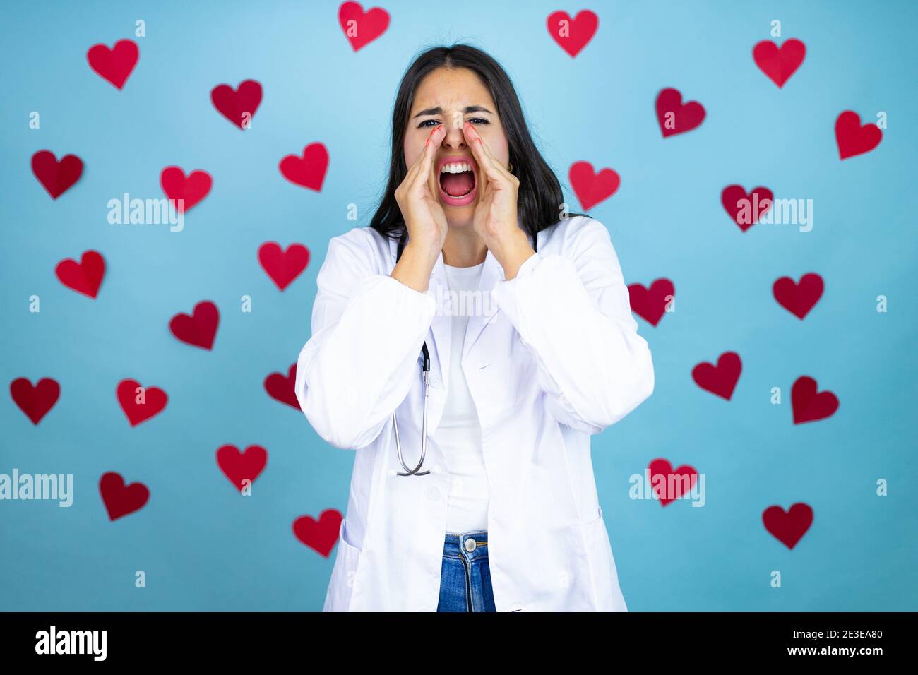 Young doctor woman wearing medical coat and stethoscope over blue ...