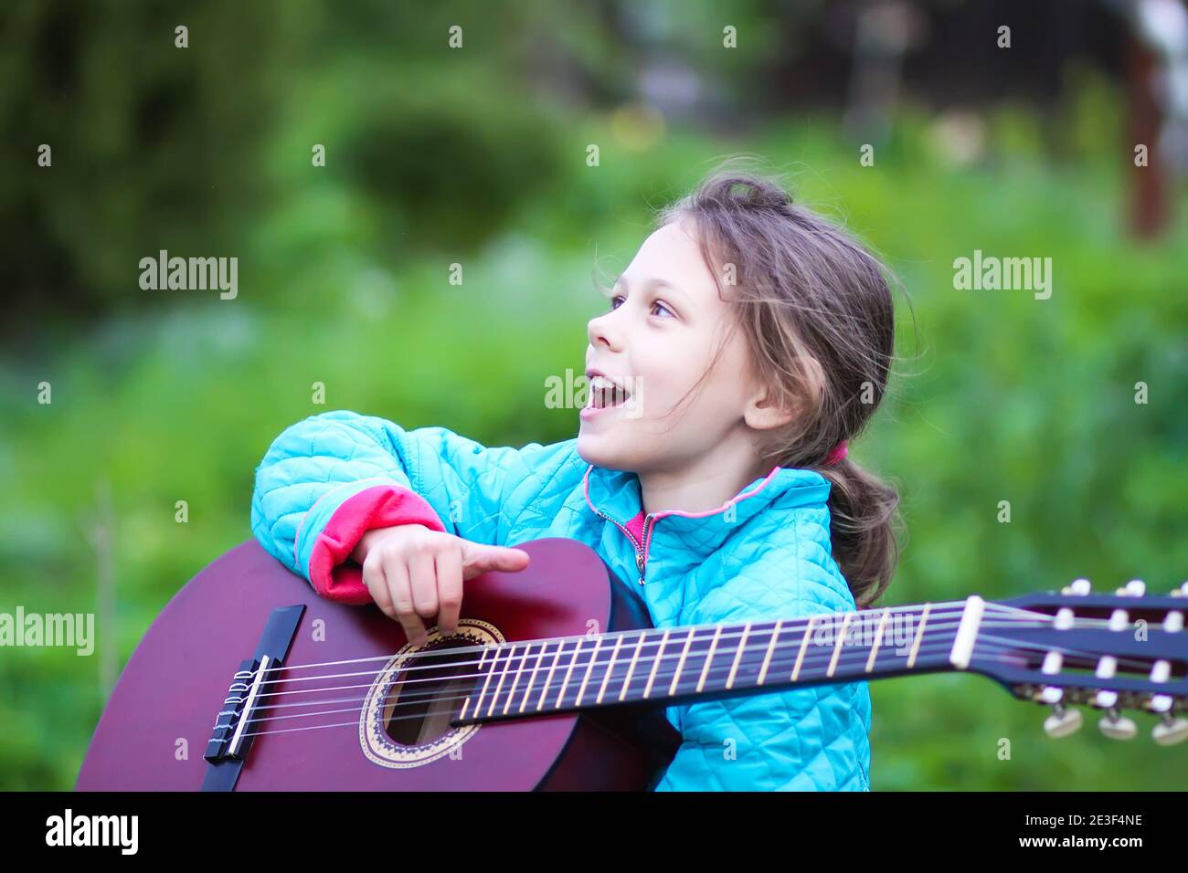 Little girl playing guitar and singing outdoors on green meadow at ...