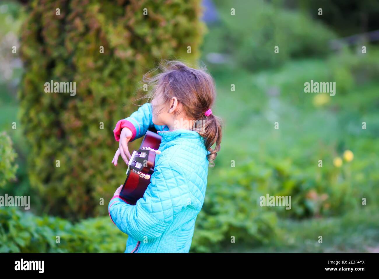 Little girl playing guitar and singing outdoors on green meadow at ...